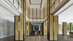 Um hall amplo com piso estampado em padrão geométrico, tetos altos com iluminação embutida e uma área de estar central.