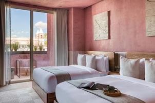 Quarto de hotel com duas camas, uma janela grande com vista para um edifício e uma varanda com uma cadeira.