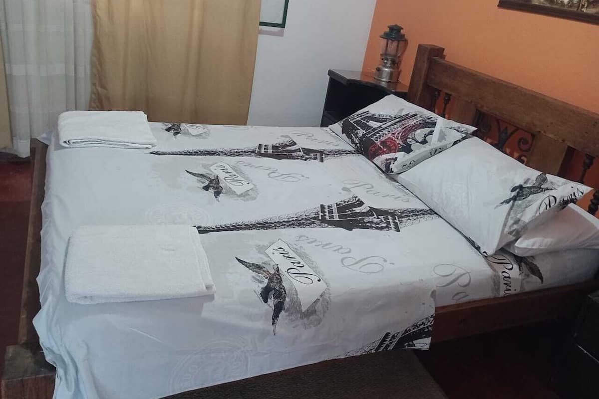 Uma cama com colcha branca estampada com pássaros e a palavra 'Paradise'.