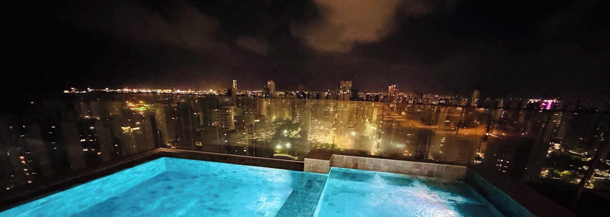 Piscina no terraço com vista para a cidade à noite.