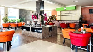 Um saguão de hotel com uma ilha central, assentos em laranja e uma parede com detalhes verdes.
