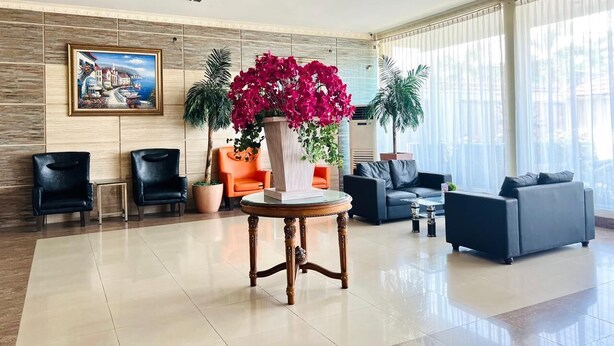 Um hall moderno com uma mesa redonda de madeira, duas cadeiras de couro preto, um sofá e uma grande janela com cortinas leves.