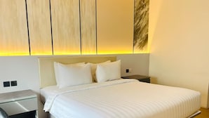 Quarto de hotel moderno com uma cama grande, mesas de cabeceira e uma luminária fixada na parede.
