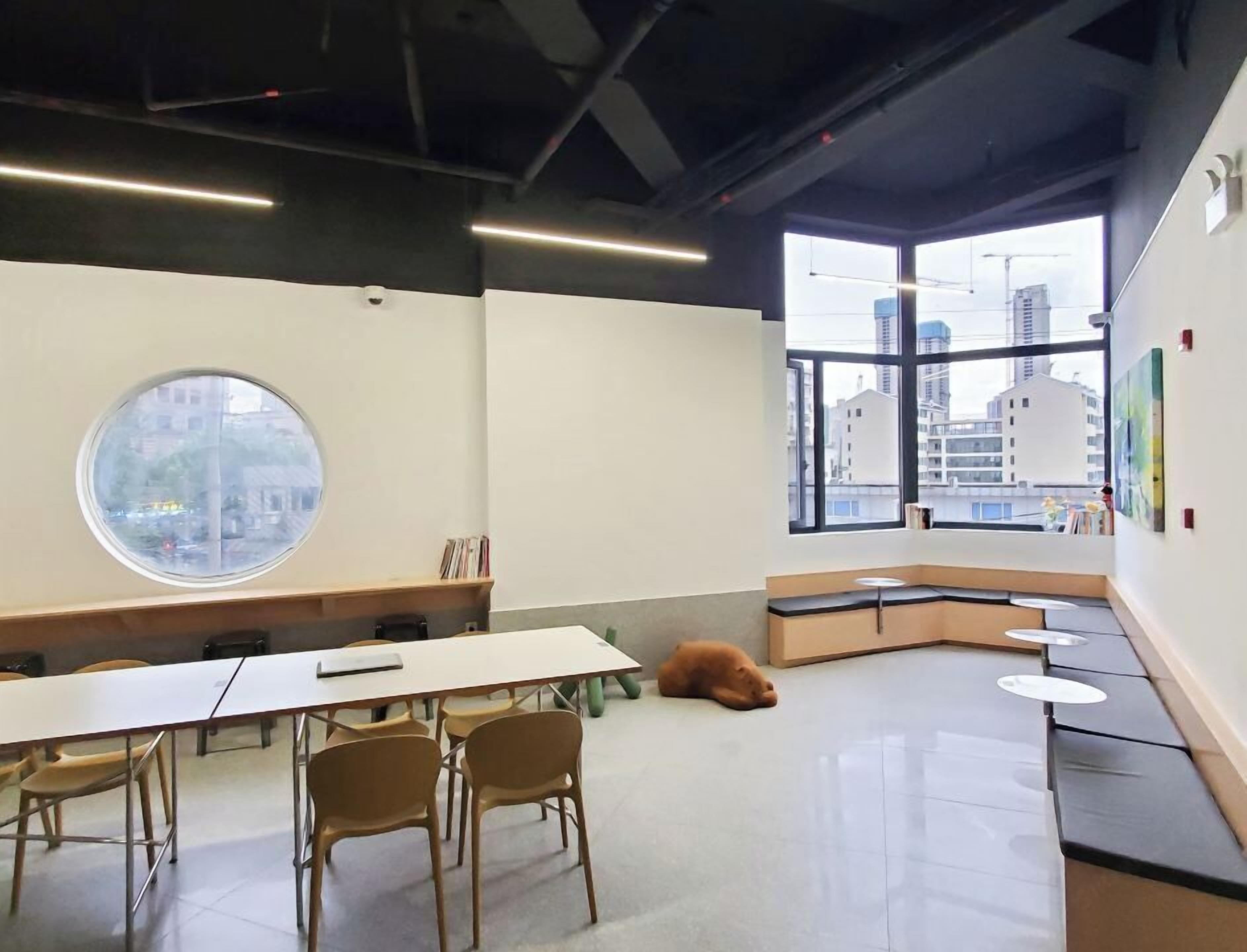 Uma sala de reuniões moderna com uma mesa comprida, cadeiras, uma janela redonda e um banco.