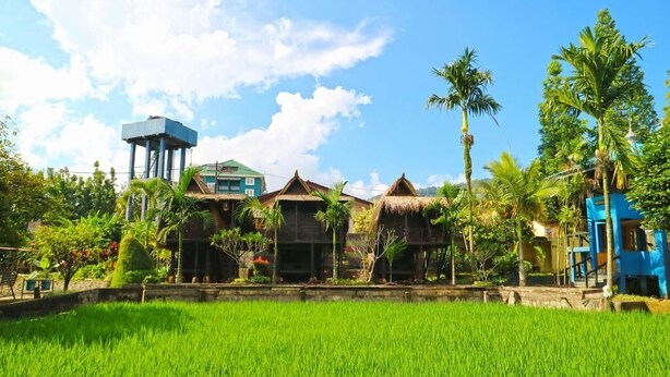 Uma casa tradicional com um reservatório de água, rodeada por vegetação exuberante e um campo de arroz.
