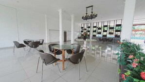 Um espaço amplo e bem iluminado, com uma mesa de vidro redonda cercada por cadeiras, janelas grandes com molduras pretas e um lustre.