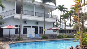 Um hotel com piscina, duas espreguiçadeiras azuis e dois guarda-sóis vermelhos.