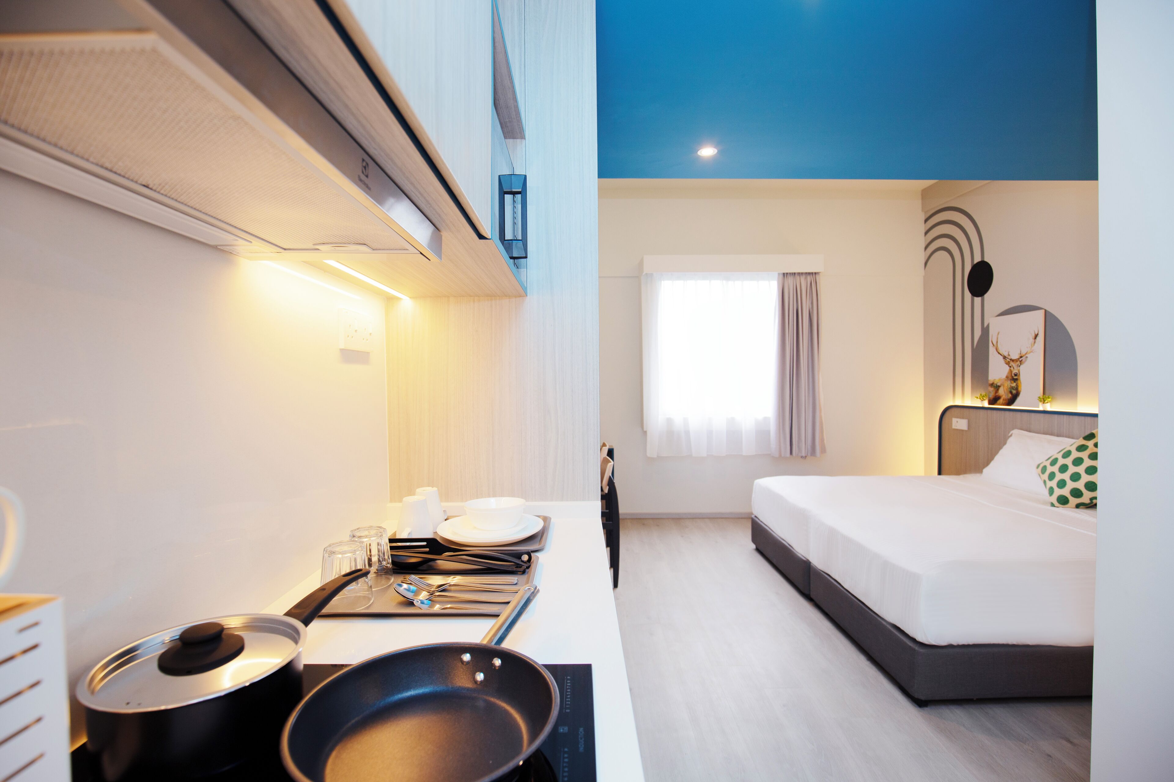 Quarto de hotel com cama, área de jantar com mesa e cadeiras, janela com cortinas e uma obra de arte na parede.