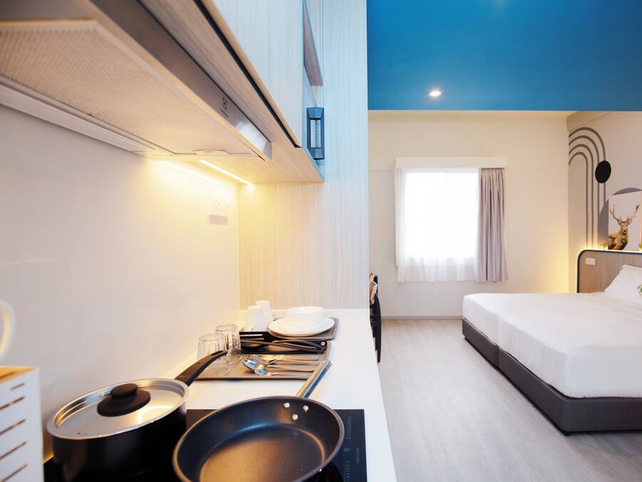 Quarto de hotel com cama, área de jantar com mesa e cadeiras, janela com cortinas e uma obra de arte na parede.