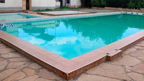 Piscina retangular com borda de pedra, rodeada por um terraço de pedra.