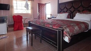 Um quarto com cama, um banquinho, uma TV e um candelabro.