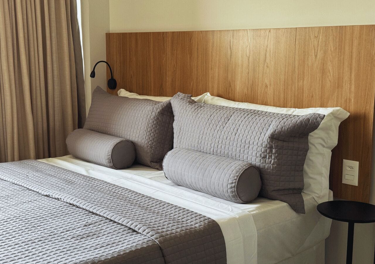 Uma cama bem arrumada com cabeceira de madeira, mesa de cabeceira e abajur.
