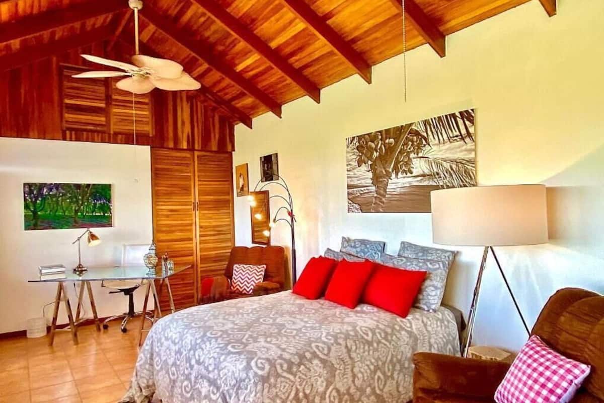 Quarto com cama, escrivaninha, cadeira e ventoinha no teto.