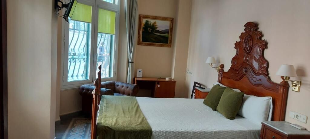 Quarto com cama de madeira, escrivaninha, cadeira e janela com cortinas.