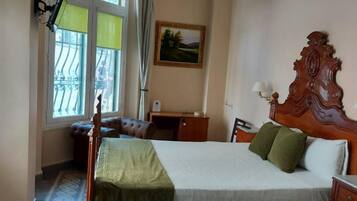 Quarto com cama de madeira, escrivaninha, cadeira e janela com cortinas.