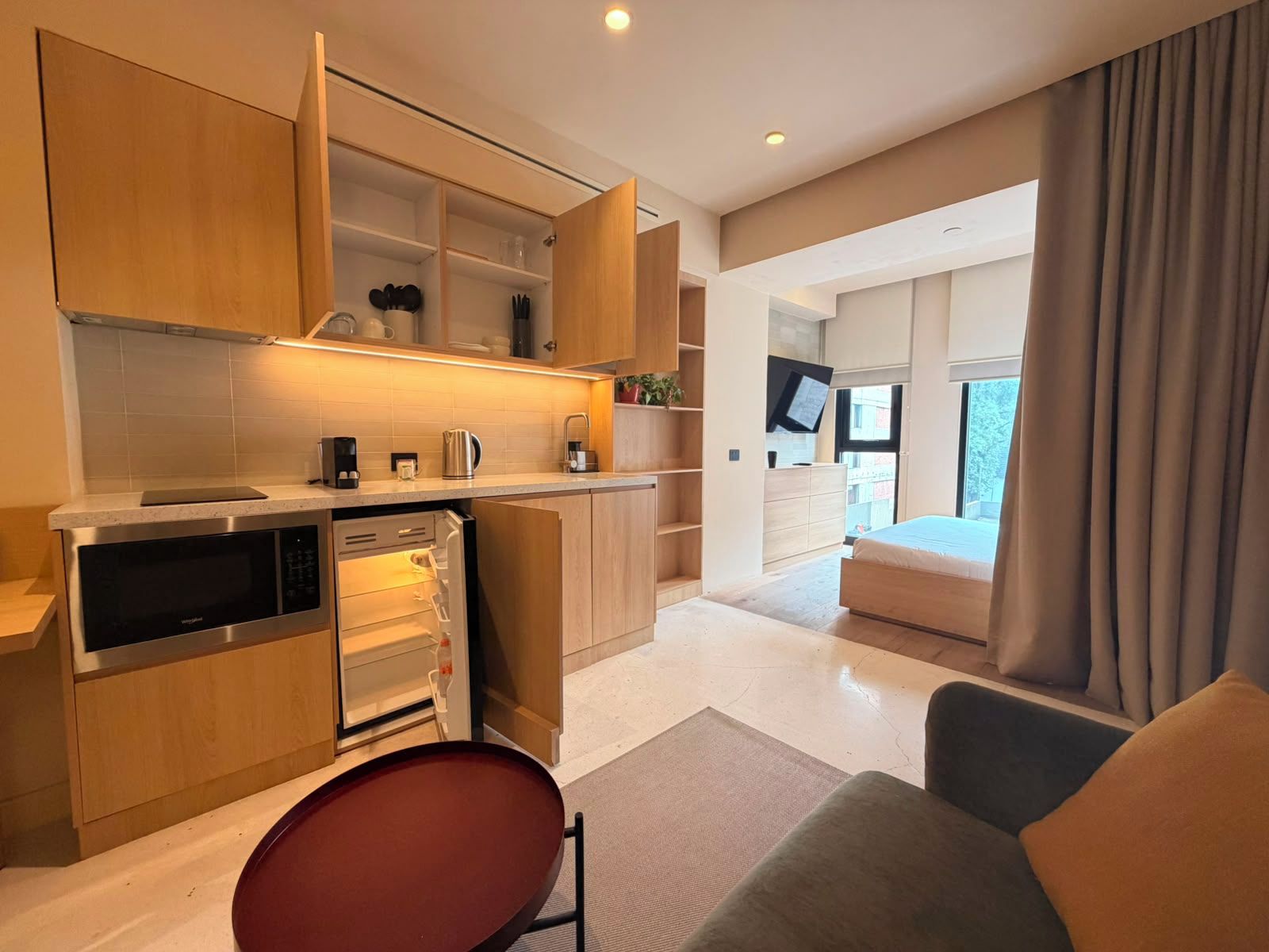 Cozinha moderna com eletrodomésticos integrados, sala de jantar com uma cadeira vermelha e sala de estar com sofá e televisão.