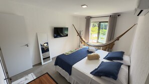 Quarto com cama, rede, televisão e janela com cortinas.