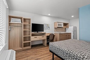 Quarto compacto com cama, escrivaninha, TV, micro-ondas e geladeira.