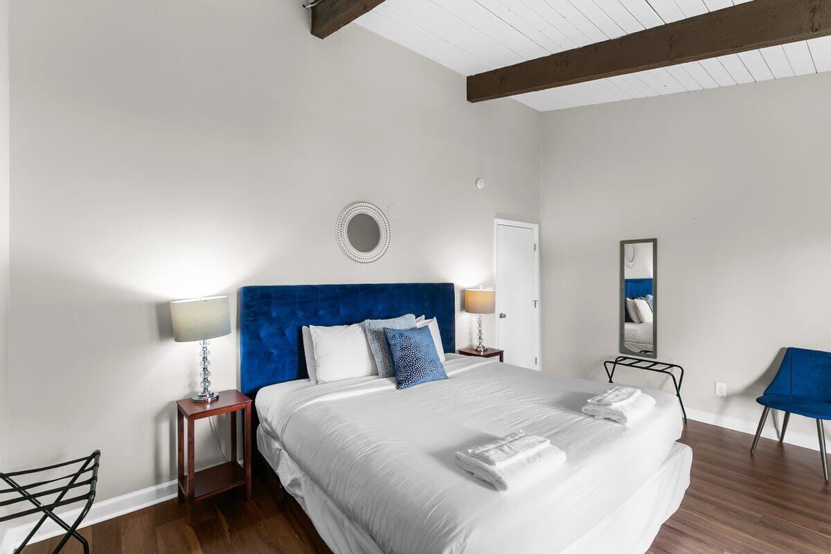 Quarto de hotel com uma cama grande, duas mesas de cabeceira com luminárias, uma cadeira e um espelho na parede.