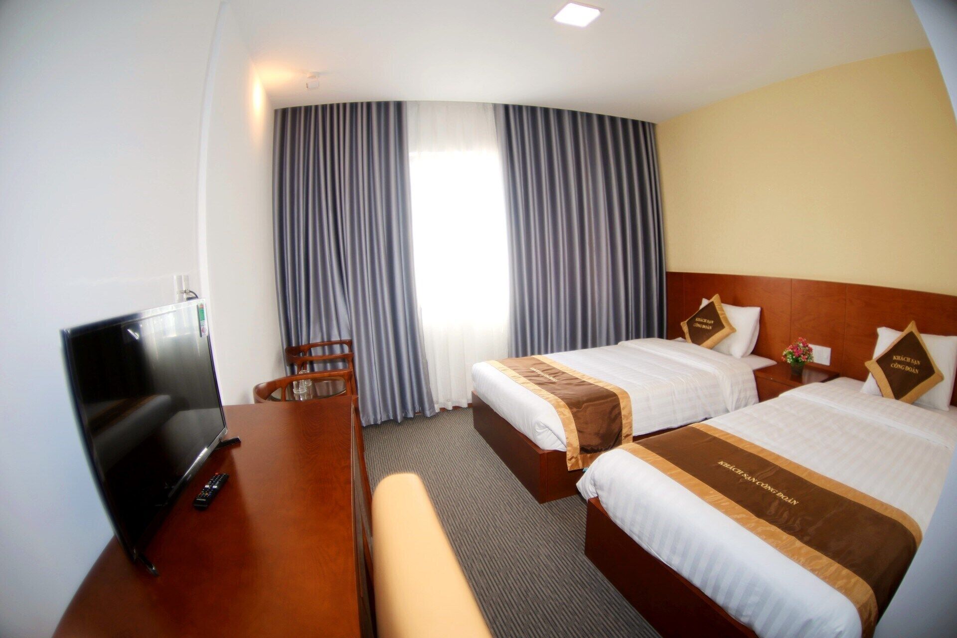 Quarto de hotel com duas camas, uma escrivaninha com televisão e uma cadeira.