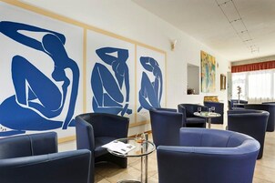 Um hall de hotel moderno com arte abstrata nas paredes, assentos confortáveis e interior bem iluminado.