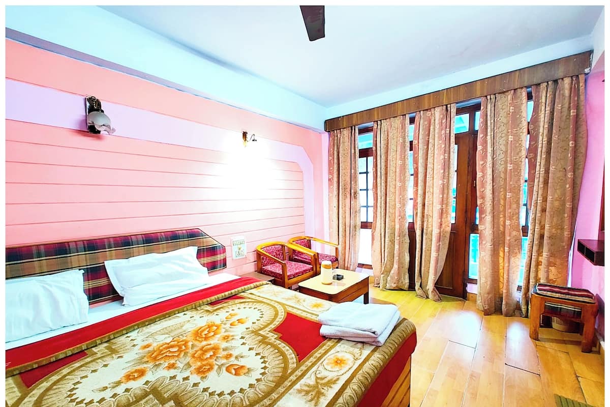 Quarto com cama, cadeira, pequena mesa e janela com cortinas.