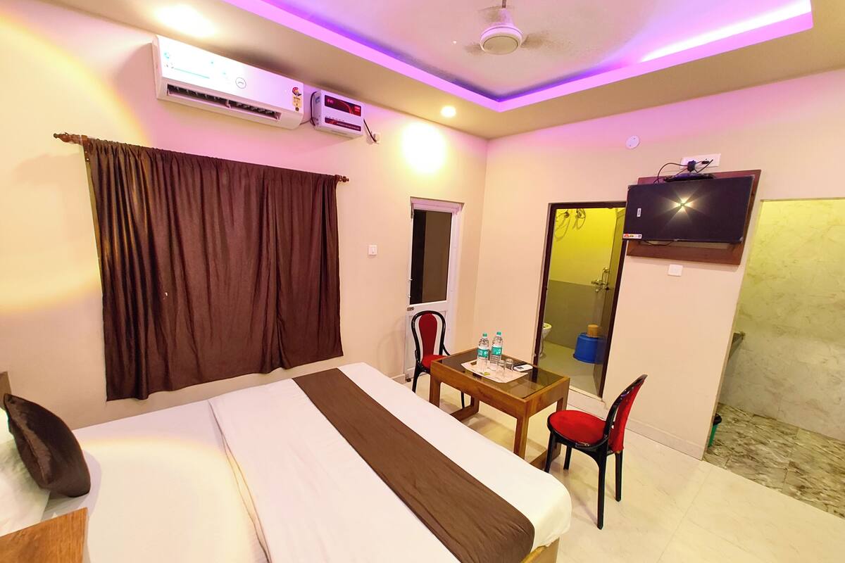 Quarto de hotel com cama, mesa e cadeiras, ar condicionado e televisão na parede.