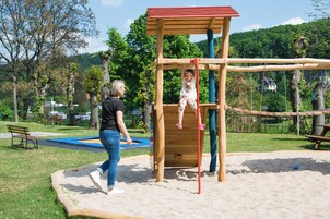 Um parquinho com uma estrutura de escalada de madeira, um caixa de areia e um banco.