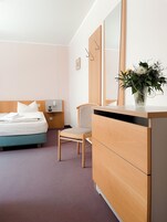 Quarto de hotel com cama, uma cadeira, cômoda e espelho.