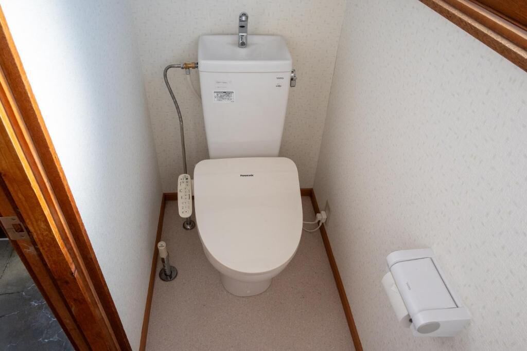 Casa de banho pequena e compacta, com sanita branca, lavatório branco e rolo de papel higiénico branco.