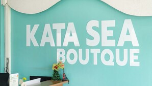 Um balcão de recepção com uma placa que diz "KATA SEA BOUTIQUE" em uma parede verde-água.