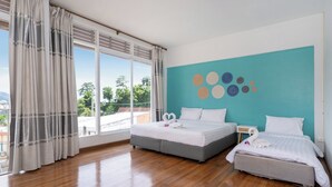 Quarto de hotel com uma cama grande, uma cama menor, vista para o exterior e uma parede de destaque azul-turquesa.