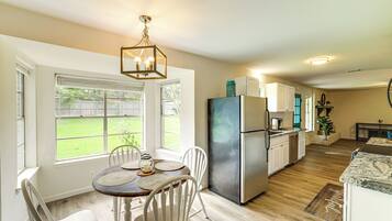 Cozinha equipada com frigorífico, mesa de jantar com cadeiras e janela com vista para um jardim.
