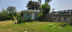 Uma casa pequena e térrea com fachada verde, porta da frente e quintal cercado.