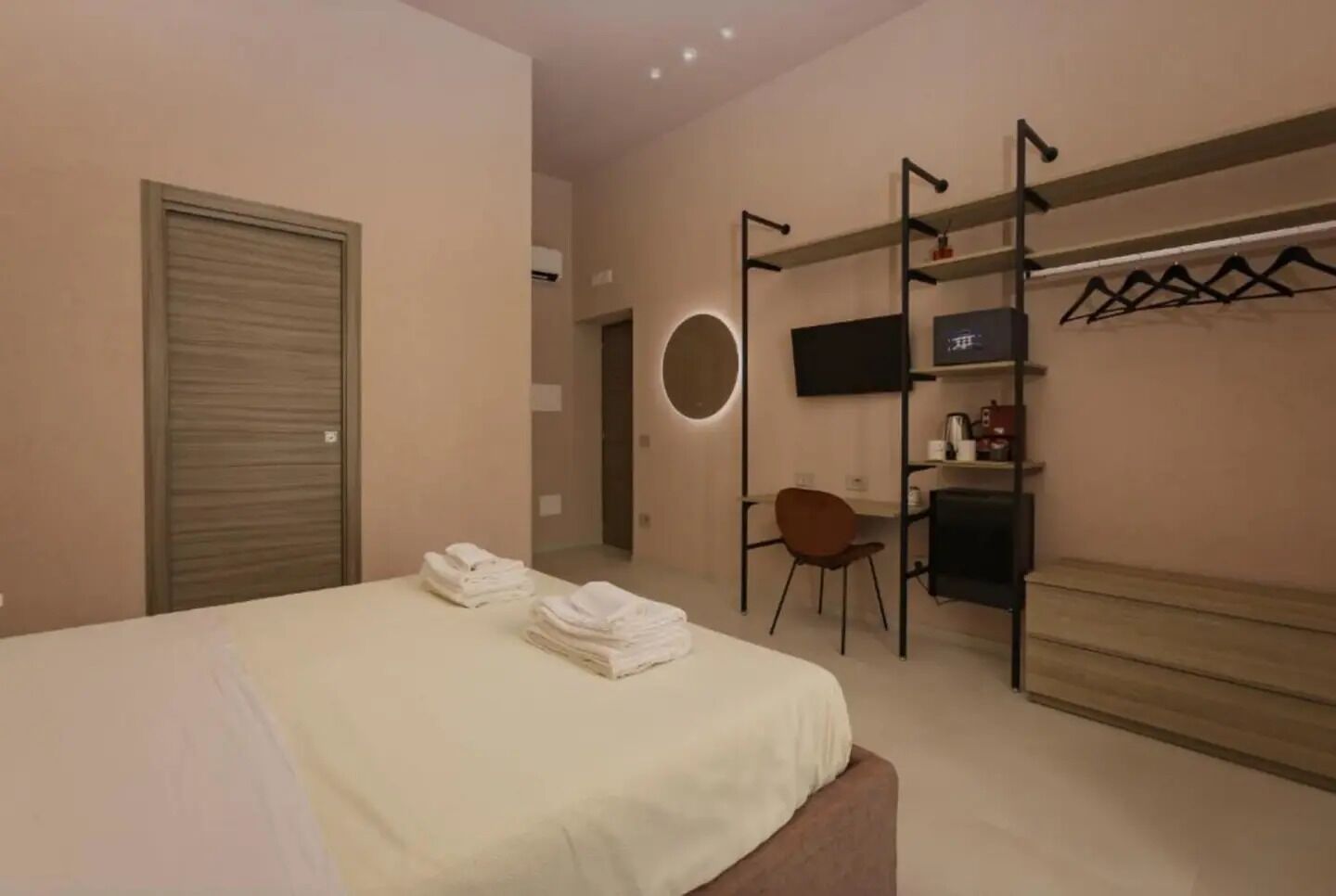 Quarto de hotel moderno com uma cama, uma poltrona, uma televisão e um cabideiro.