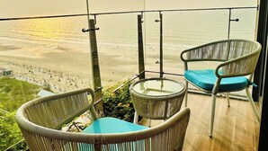 Varanda com cadeiras de vime e mesa de vidro, com vista para a praia.