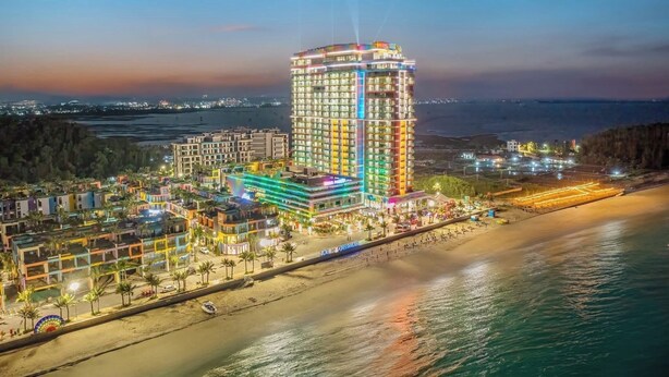 Um hotel moderno e alto, com vários andares, localização à beira-mar e um calçadão bem iluminado.