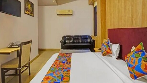 Quarto de hotel com cama, escrivaninha, cadeira, sofá e televisão na parede.