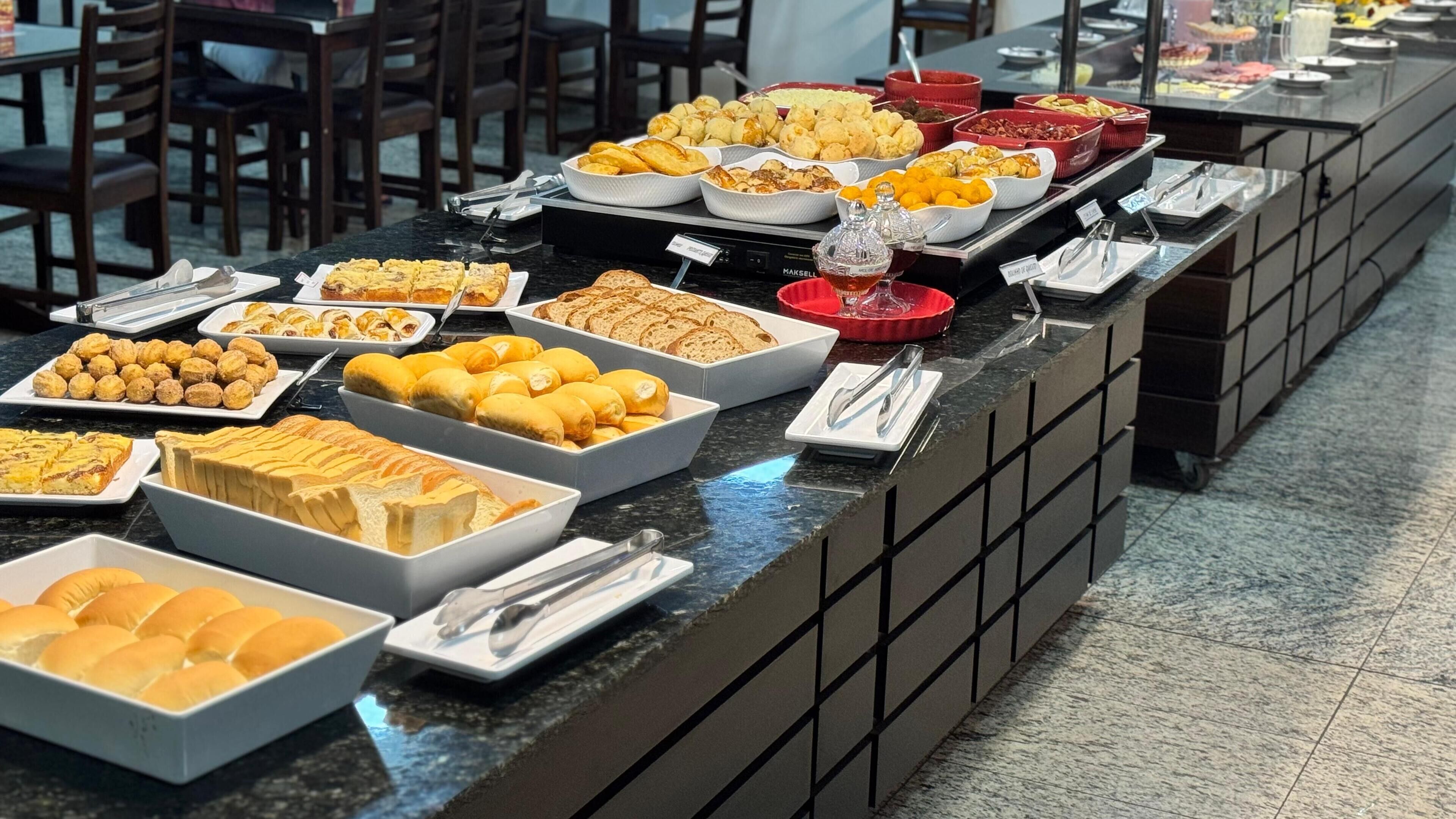 Buffet com diversos alimentos, incluindo doces, frutas e pão.