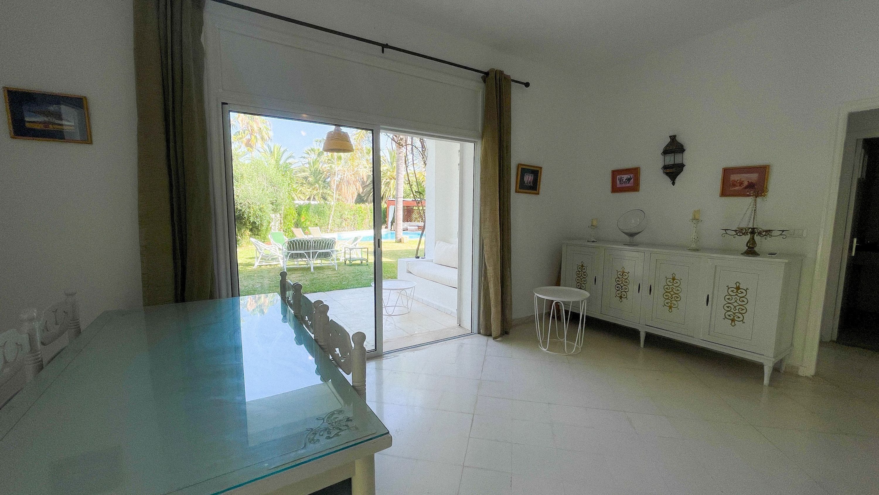 Quarto com porta de vidro que dá para área externa, armário branco com puxadores decorativos e uma pequena mesa redonda.