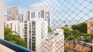 Visão através de uma cerca de arame de edifícios altos, uma rua com veículos e um corpo d'água ao longe.