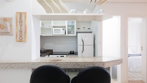 Cozinha moderna com eletrodomésticos brancos, bancada de granito e uma área de refeições visível com uma cadeira preta.