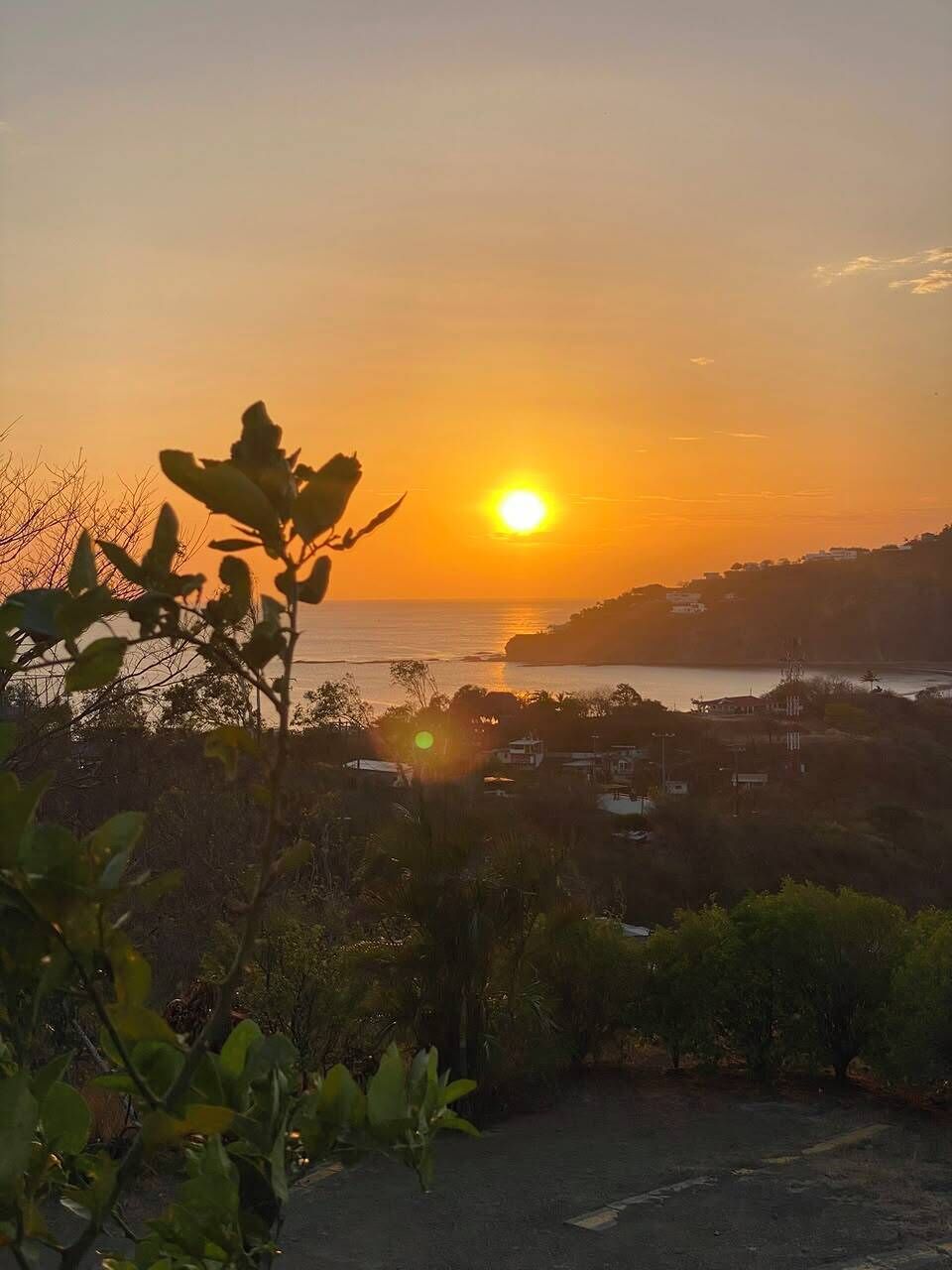 Pôr do sol sobre uma cidade costeira com edifícios e vegetação visíveis.