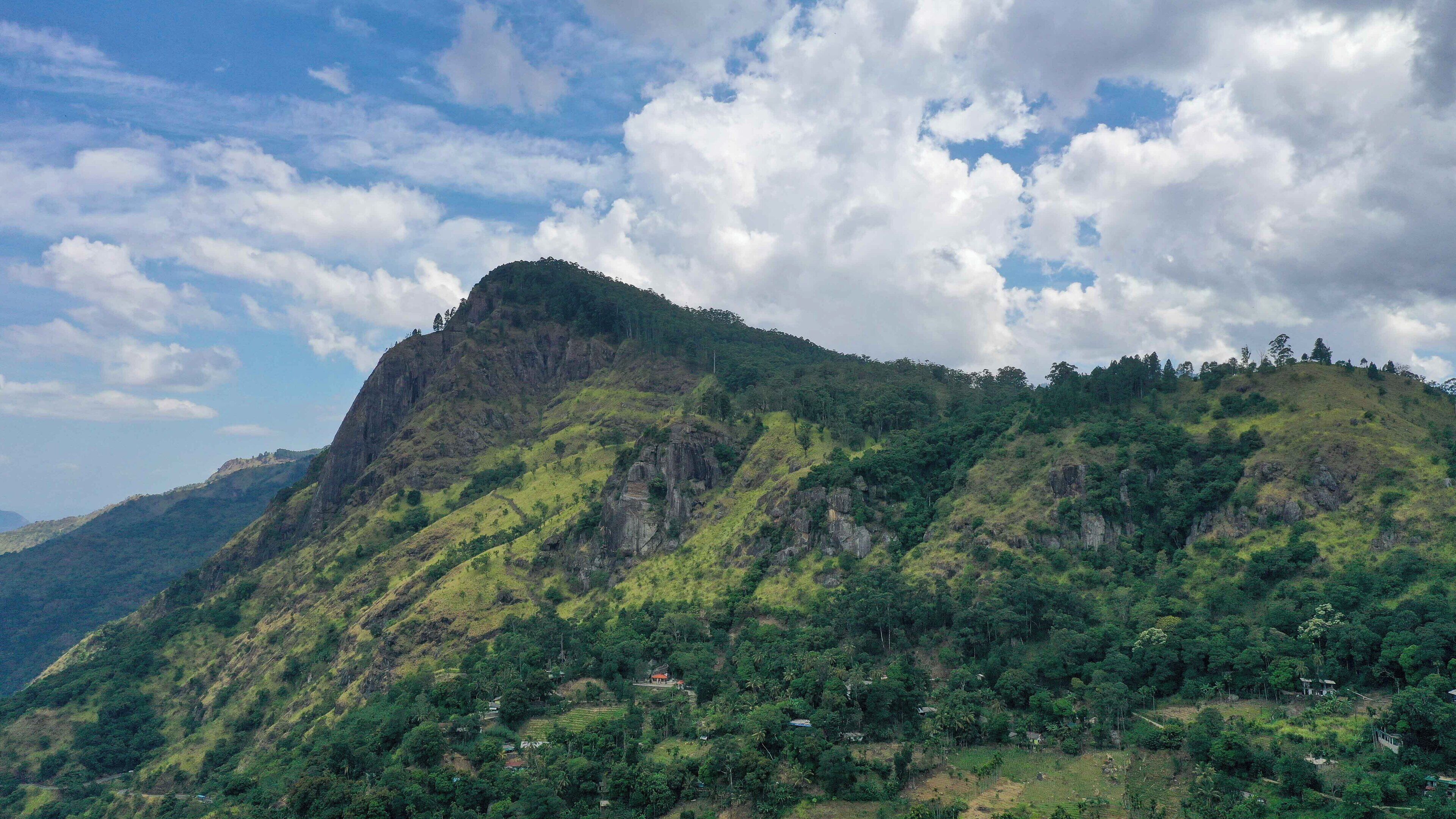 Paisagem montanhosa com pico imponente, vegetação exuberante e edifícios dispersos.