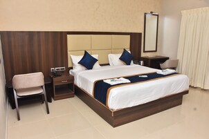 Quarto de hotel com uma cama grande, mesa de cabeceira com abajur, uma cadeira e um espelho na parede.