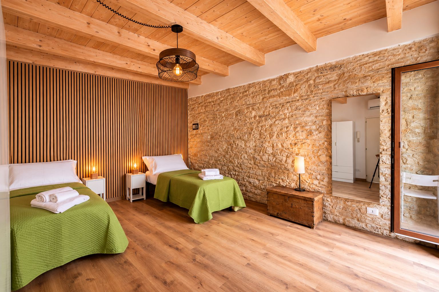 Quarto de hotel com duas camas, pisos de madeira, parede de pedra e teto de madeira.