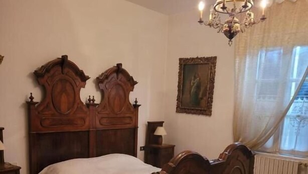Quarto com cama de madeira, um candelabro, radiador e tapetes estampados.