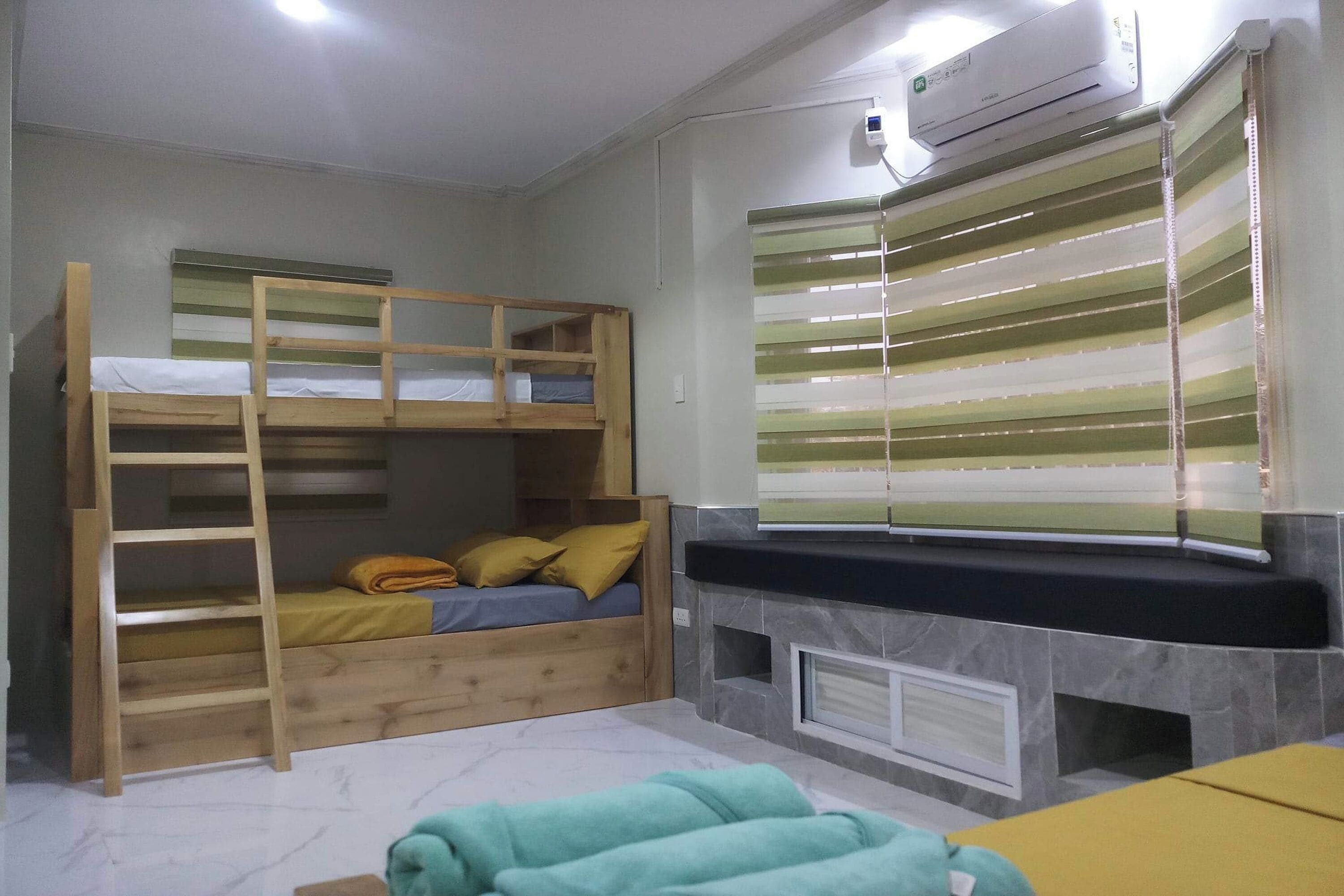 Quarto com beliches, uma pequena escrivaninha e janela com persianas.