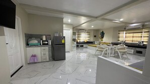 Uma cozinha moderna com piso de mármore branco, geladeira e área de refeições com cadeiras brancas.