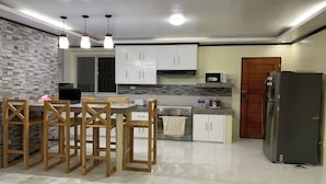 Uma cozinha moderna com armários brancos, um espaço de refeições com cadeiras de madeira, uma geladeira e um micro-ondas.